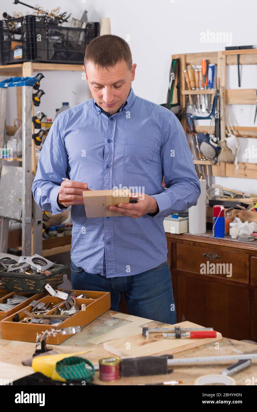positive young spanish male carpenter working wood plank at workshop ...