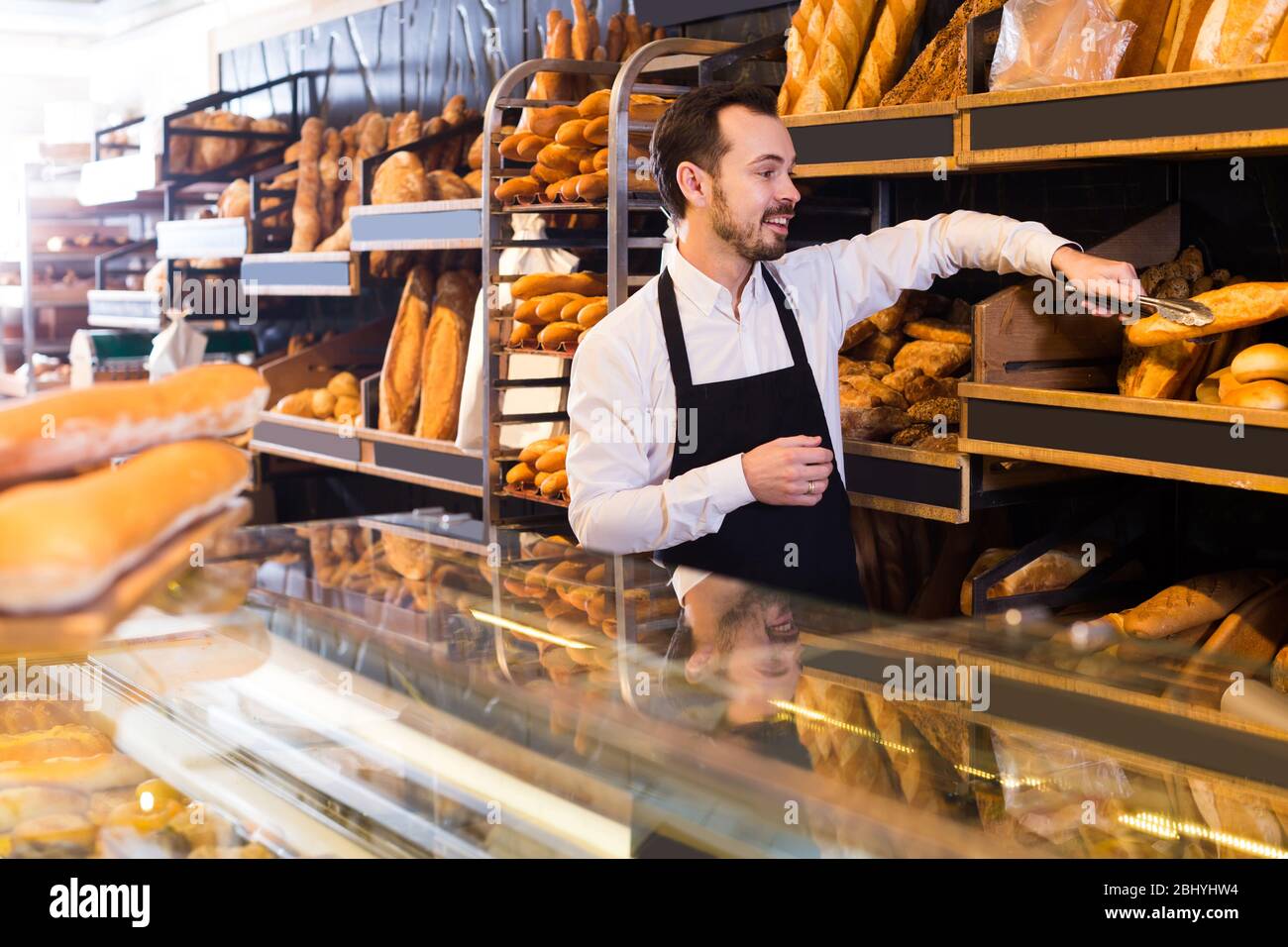 Positive European Male Shop Assistant Demonstrating Delicious Loaves Of