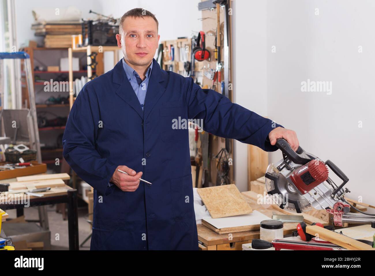 Portrait of positive adult handsome woodworker in workwear in garage ...