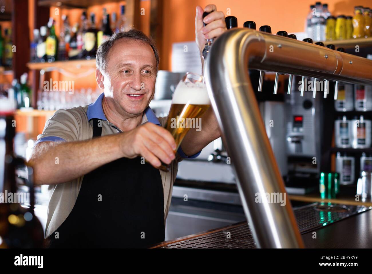 Smiling happy positive barman is pouring unbottled beer with foam for ...