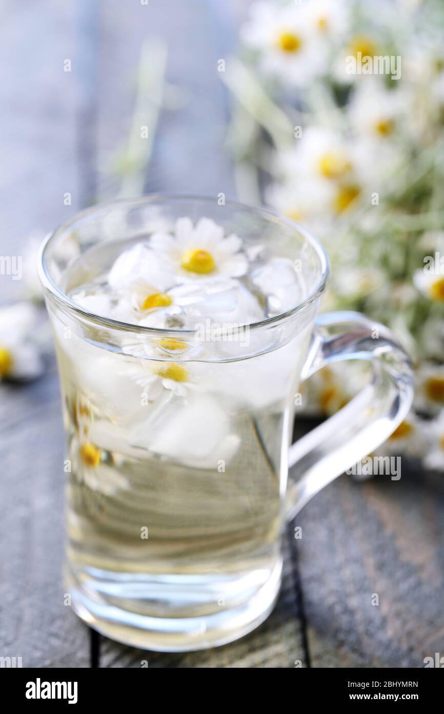 Glass of cold chamomile tea with ice cubes and chamomile flowers on ...