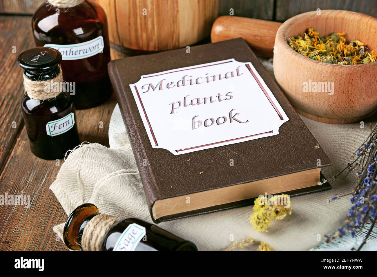 Medicinal plants book with dried herbs and bottles on table close up ...