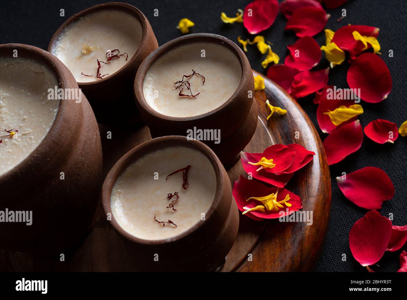 Kullads of mishti dahi kept on a wooden plate with petals around it ...