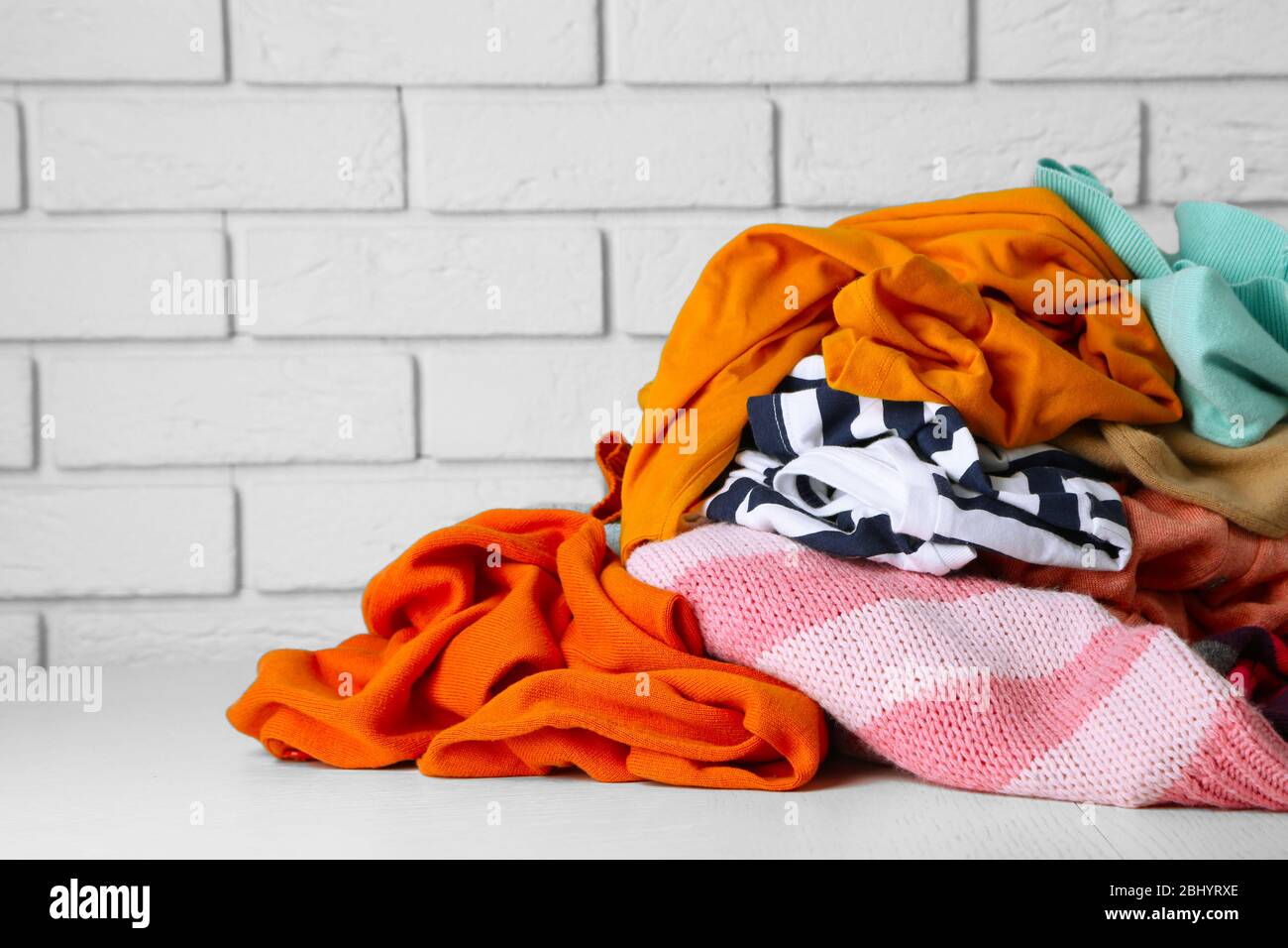 Heap of different clothes on wooden table, on bricks wall background ...