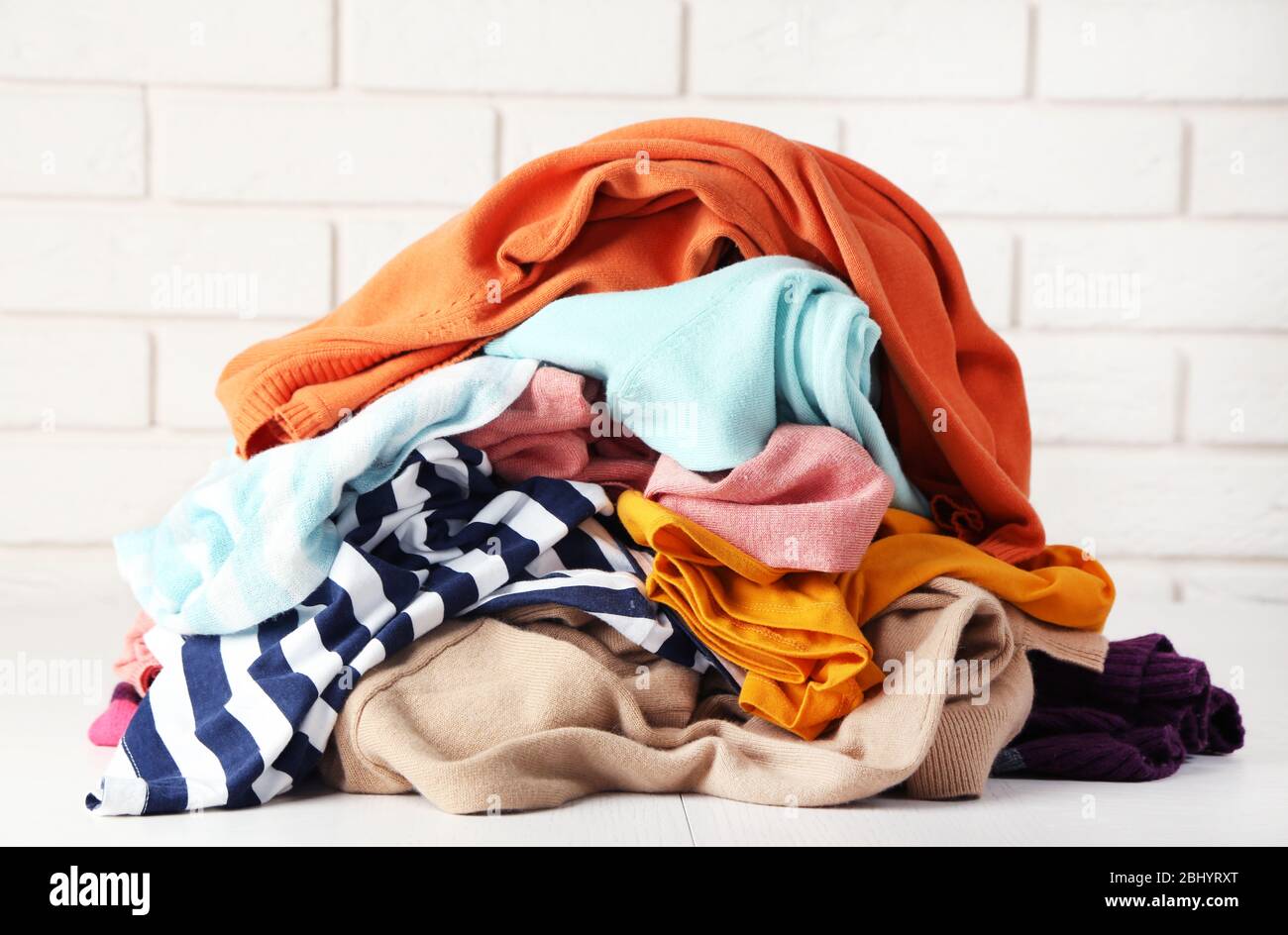 Heap of different clothes on wooden table, on bricks wall background ...