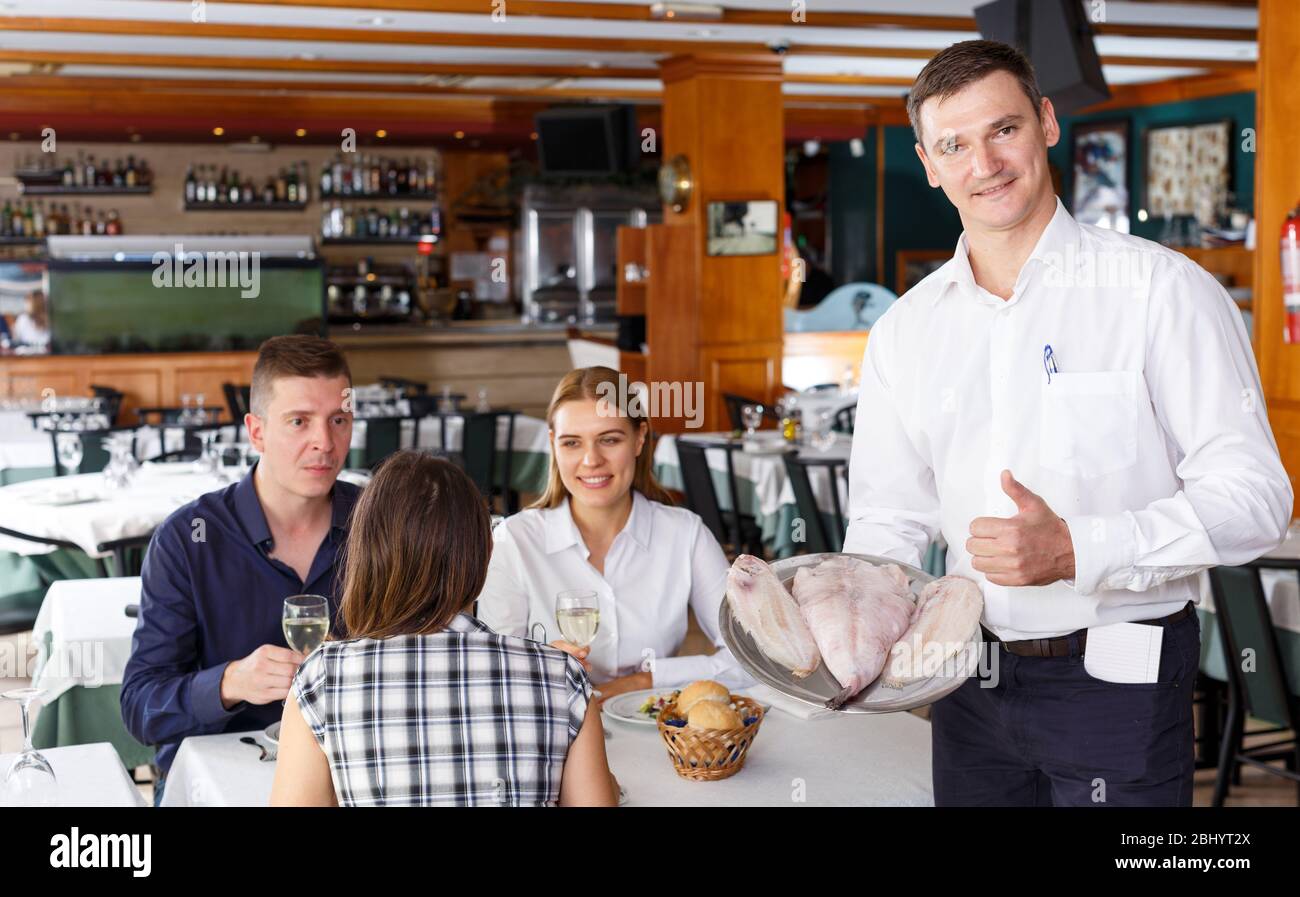 Waiter in white shirt showing tray of fish serving for group of ...