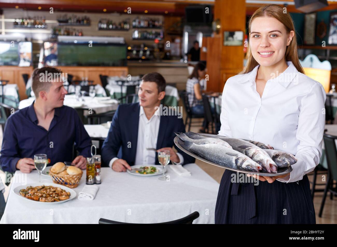 Waitress in white shirt demonstrating tray of fish serving for two male ...