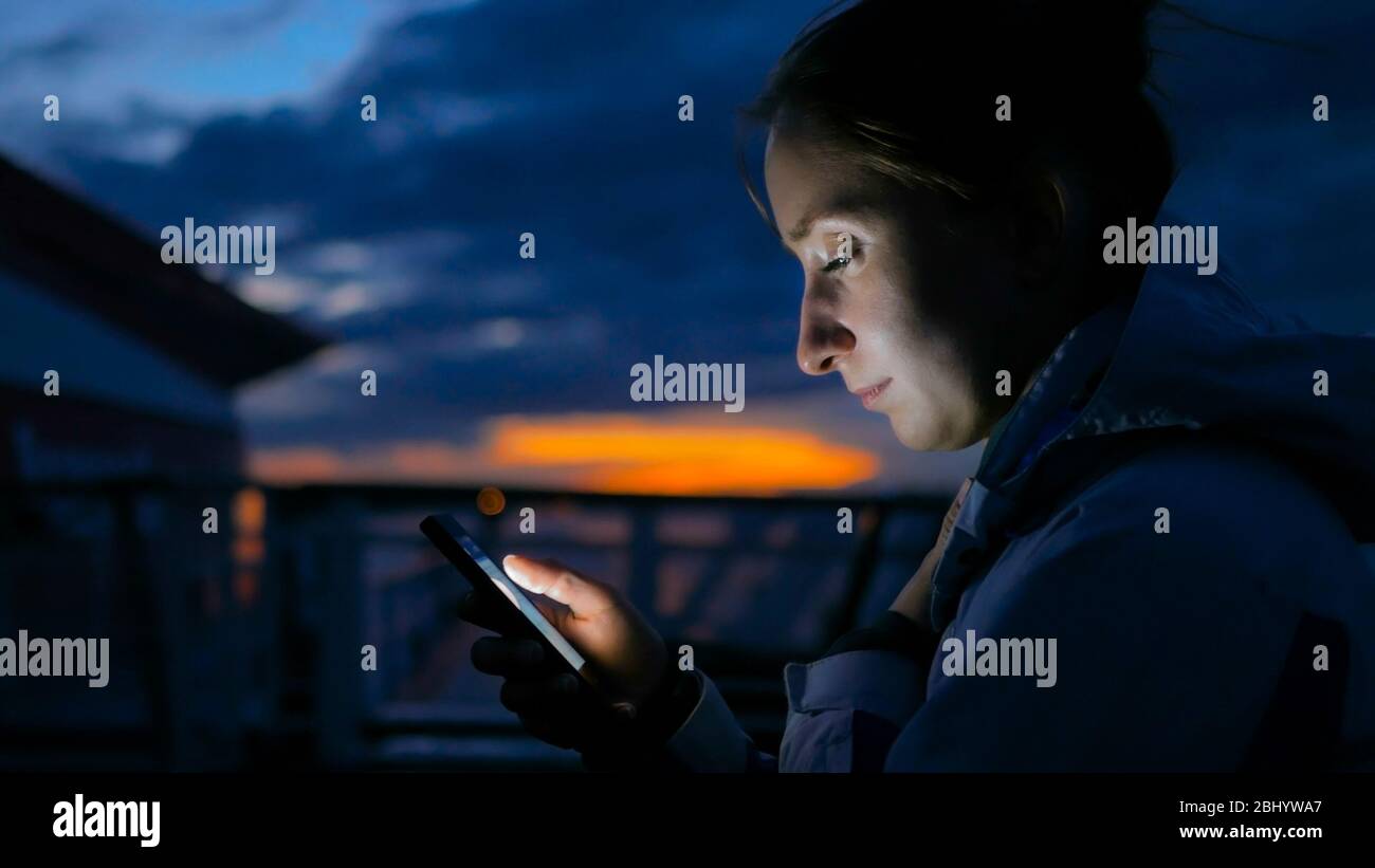 Woman using vertical smart phone on deck of cruise ship at night. Relax ...