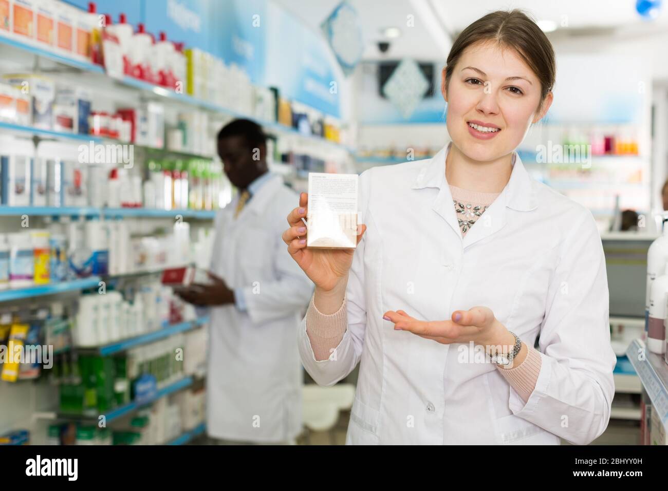 Portrait of attractive young girl pharmacist offering medication in ...