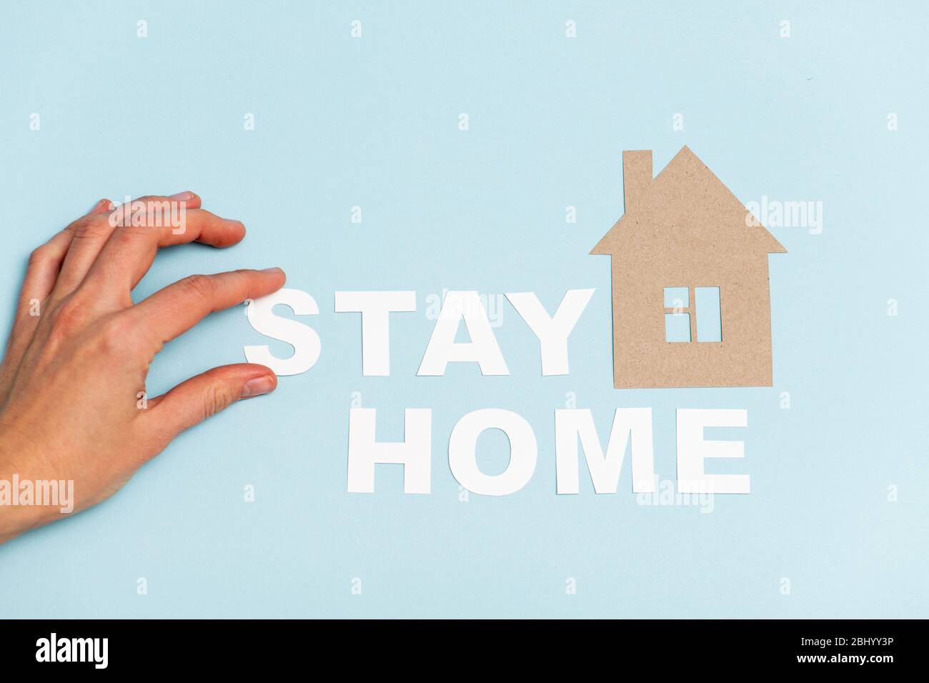 Hand placing stay home message on a blue surface next to house shape ...