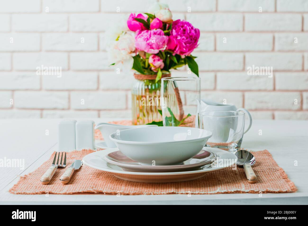 Beautiful table setting with flowers in vase on brick wall background ...
