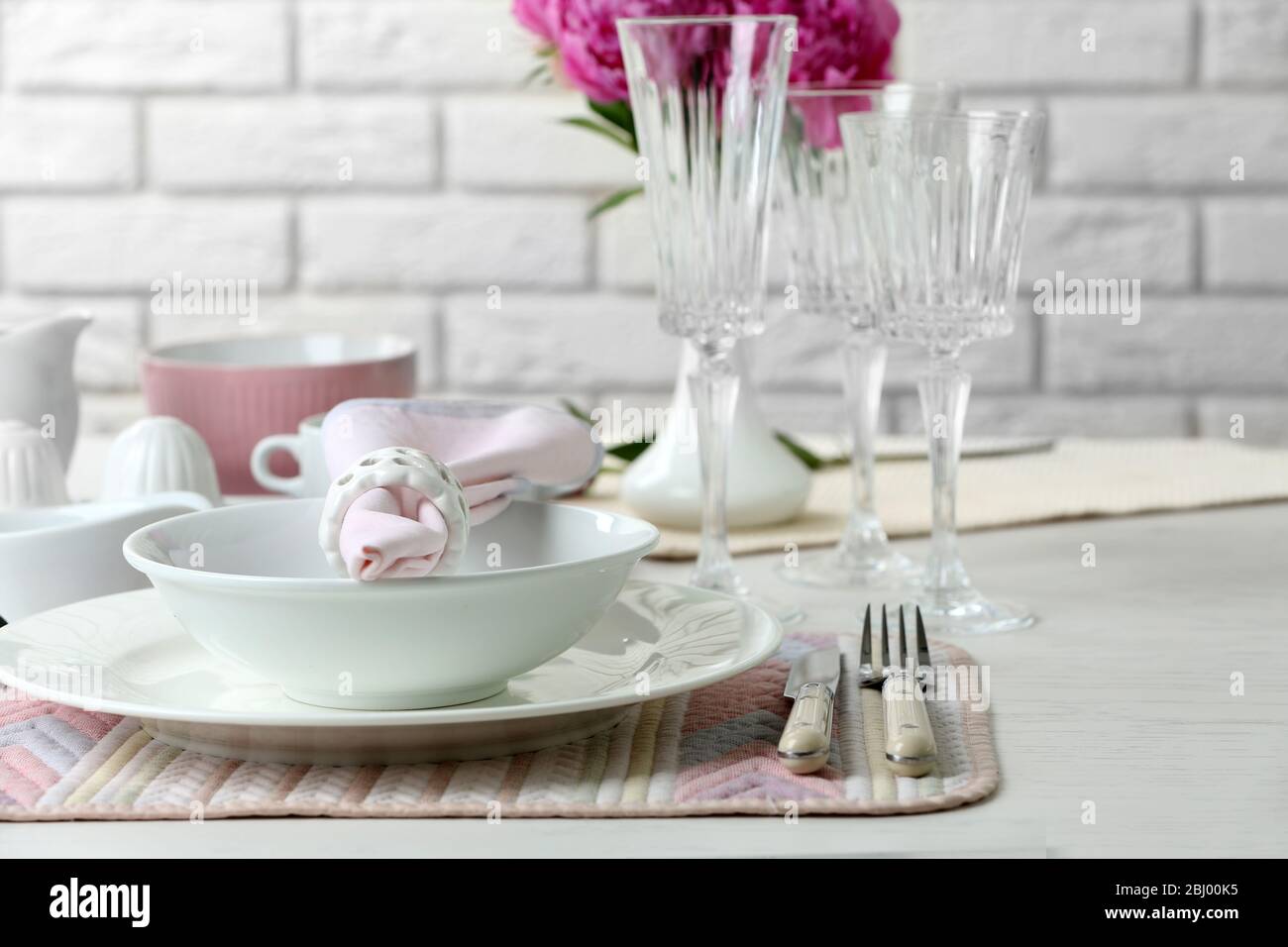 Beautiful table setting with flowers in vase on brick wall background ...