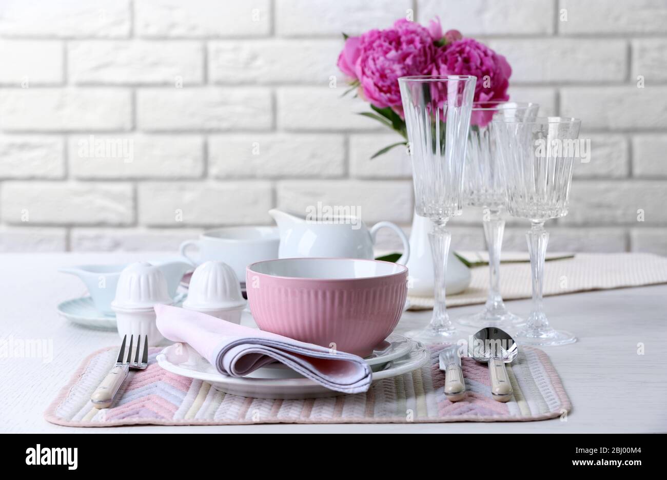 Beautiful table setting with flowers in vase on brick wall background ...
