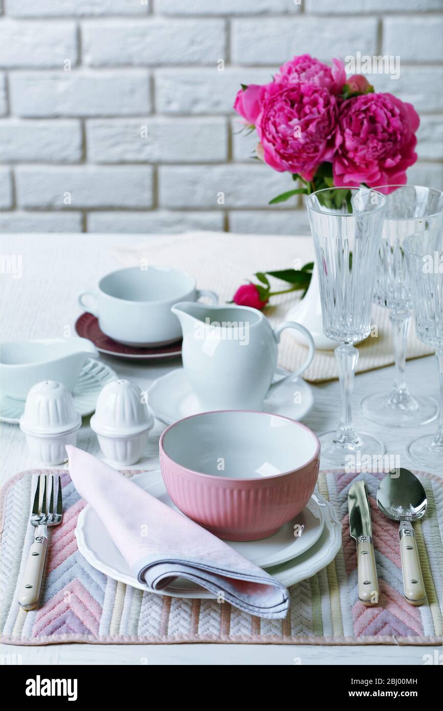 Beautiful table setting with flowers in vase on brick wall background ...