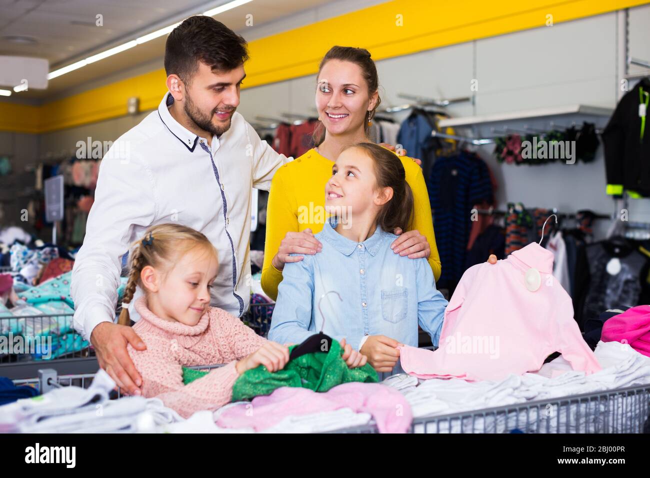 Young smiling family of four looking for children clothes on shelves in ...