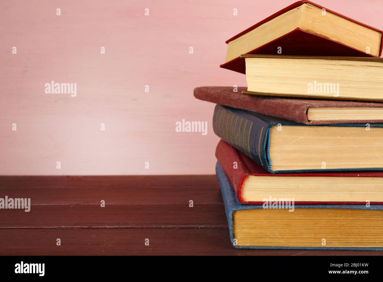 Stack of books on wooden table on pink wall background Stock Photo - Alamy