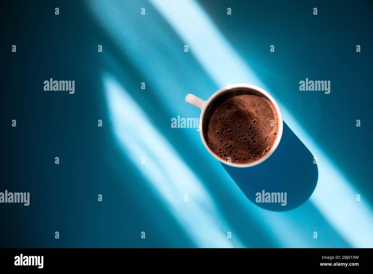 Cup of coffee on blue background. Sun rays in daylight, hard light and ...