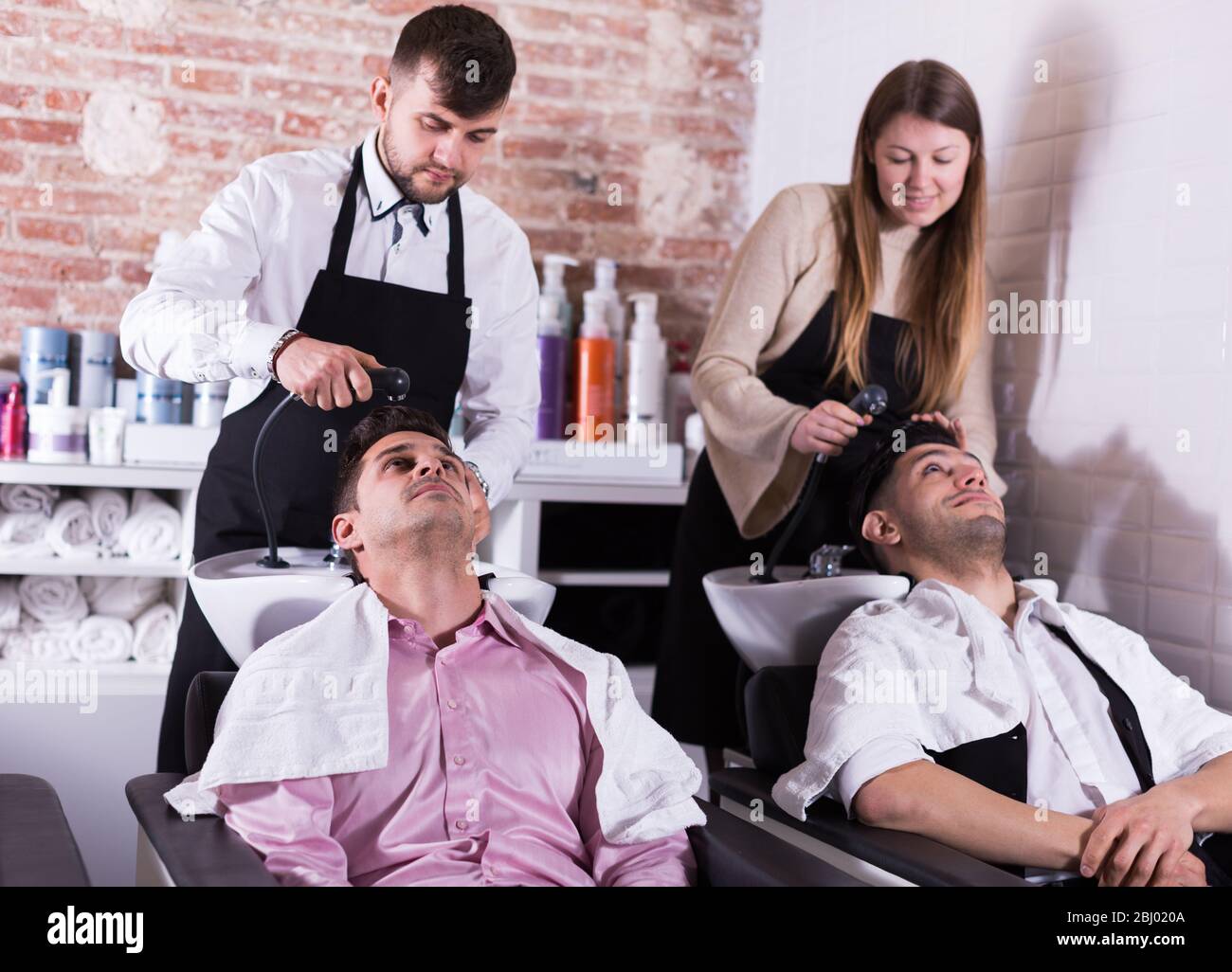 Man and woman hairdressers washing hair of male clients of modern hair ...