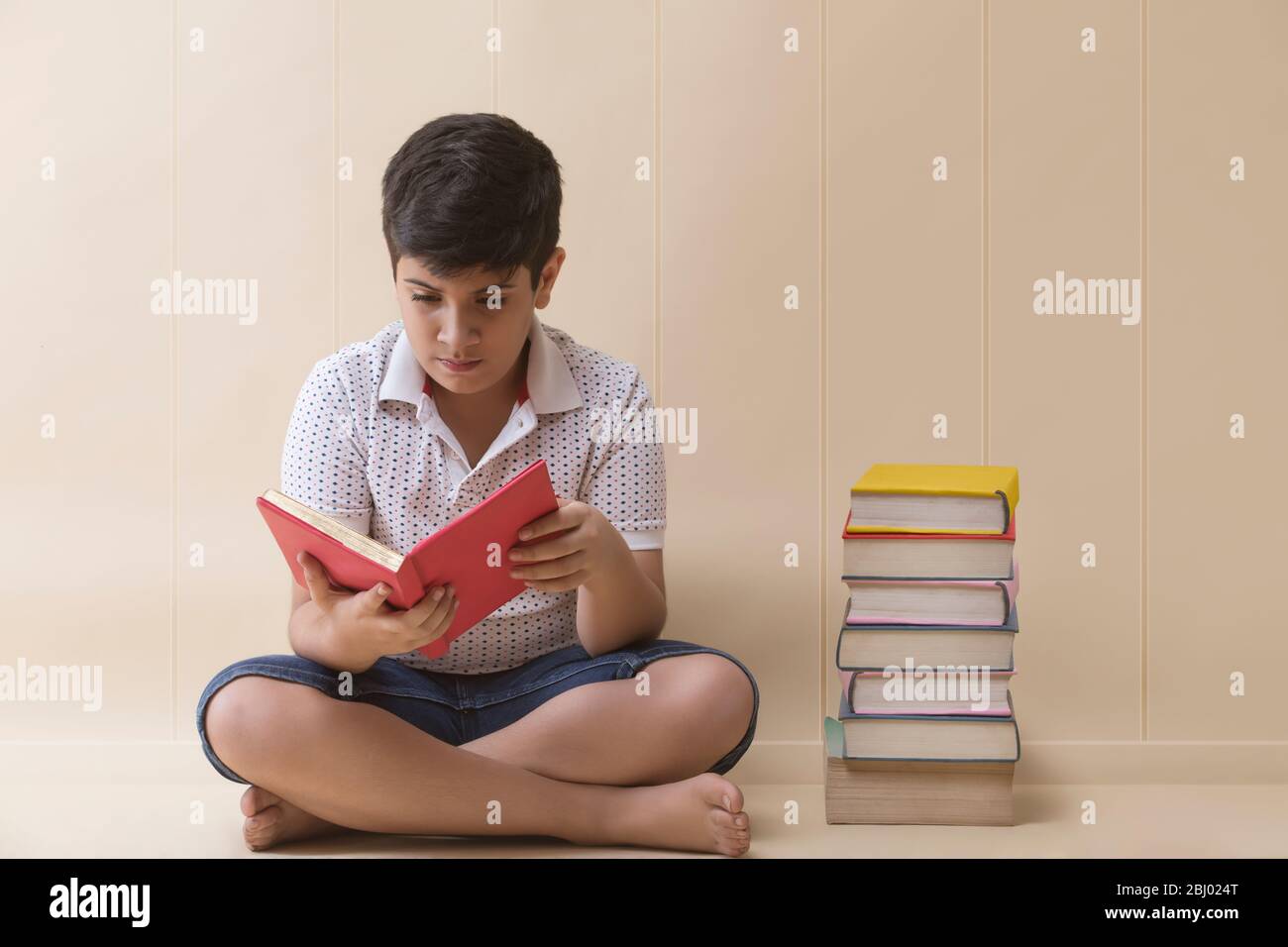 Boy Reading Book While Sitting On Floor Against Wooden Wall Stock Photo ...