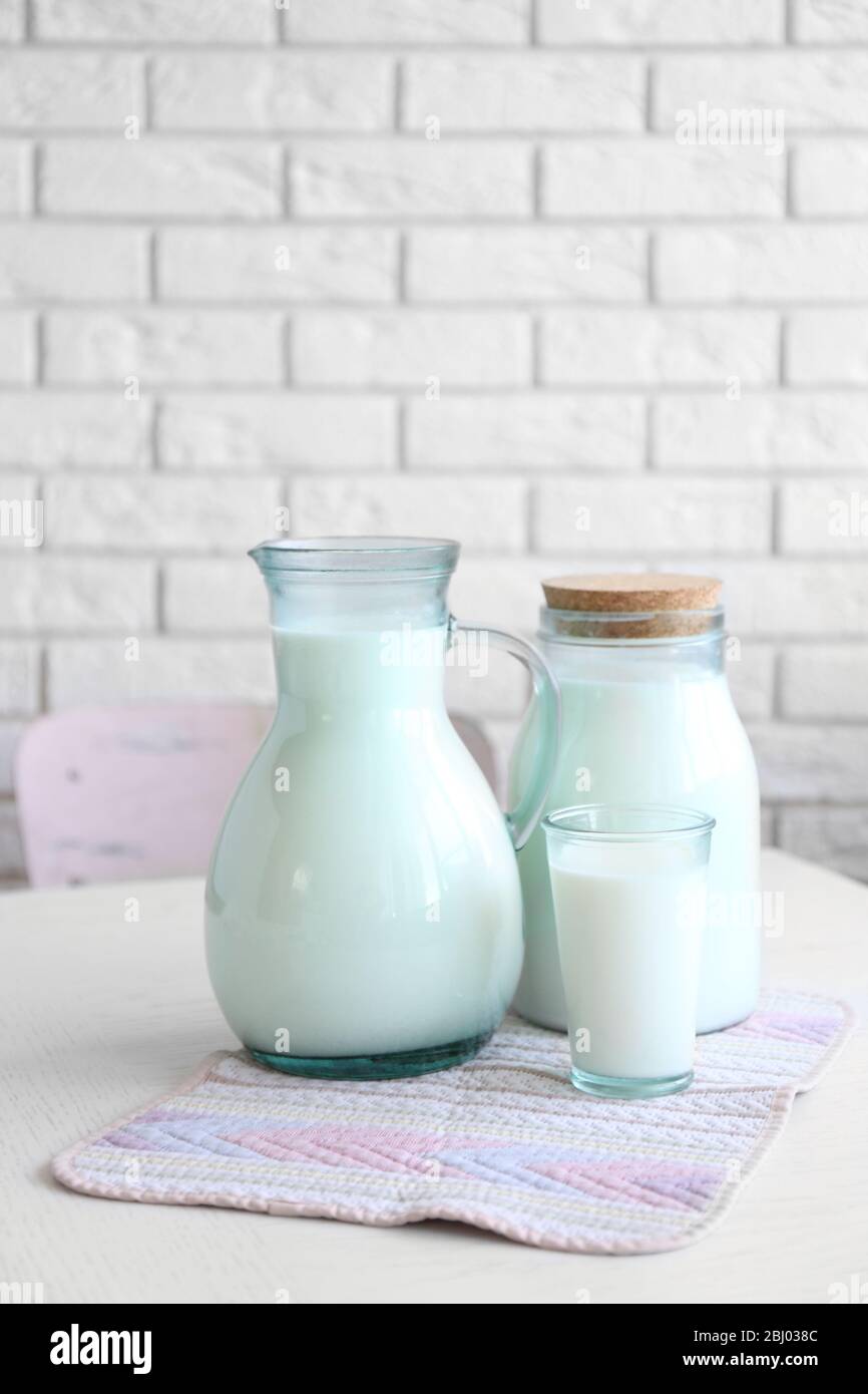 Pitcher, jar and glass of milk on wooden table, on bricks wall ...