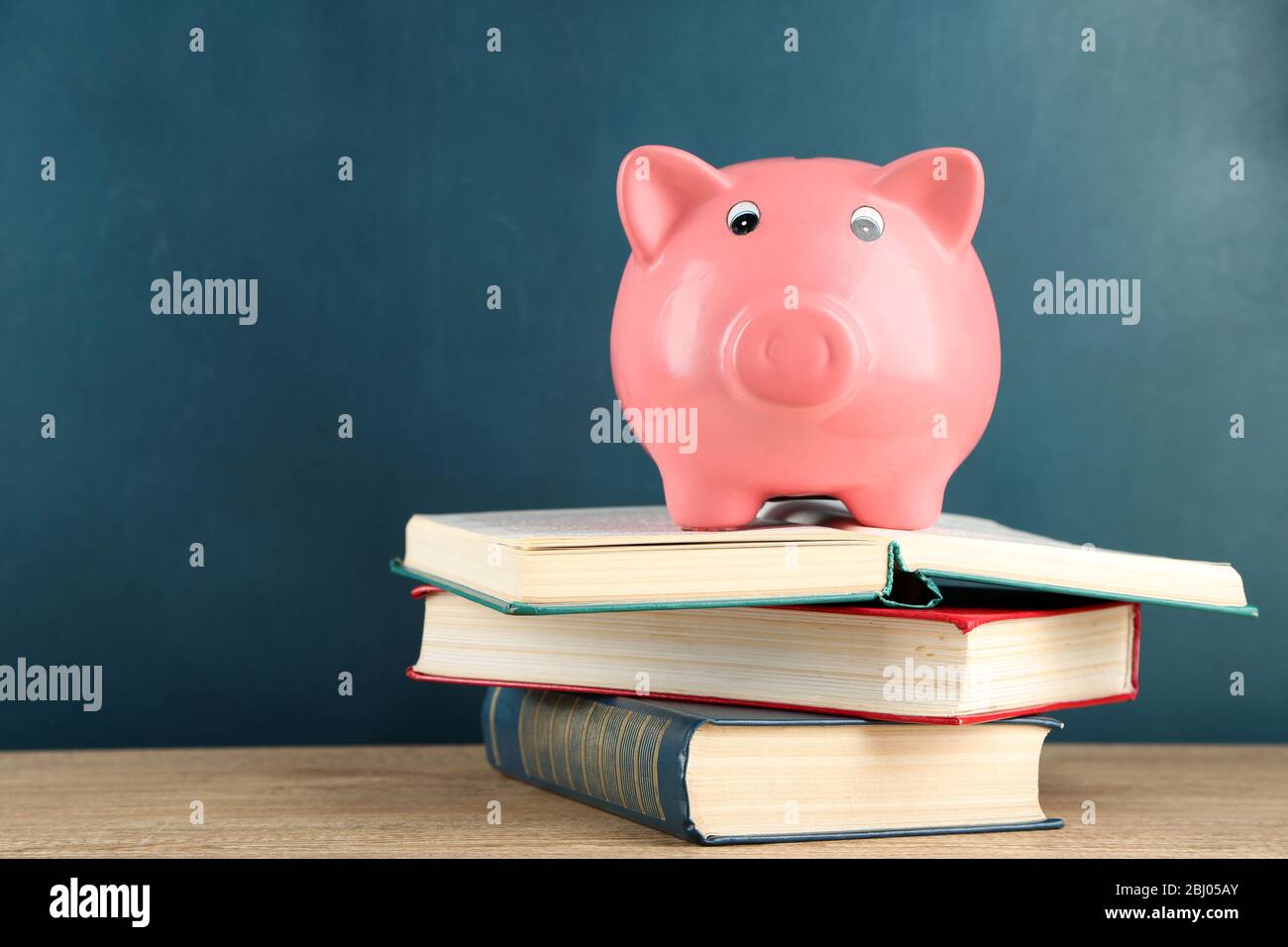 Piggy bank with books on blackboard background Stock Photo - Alamy