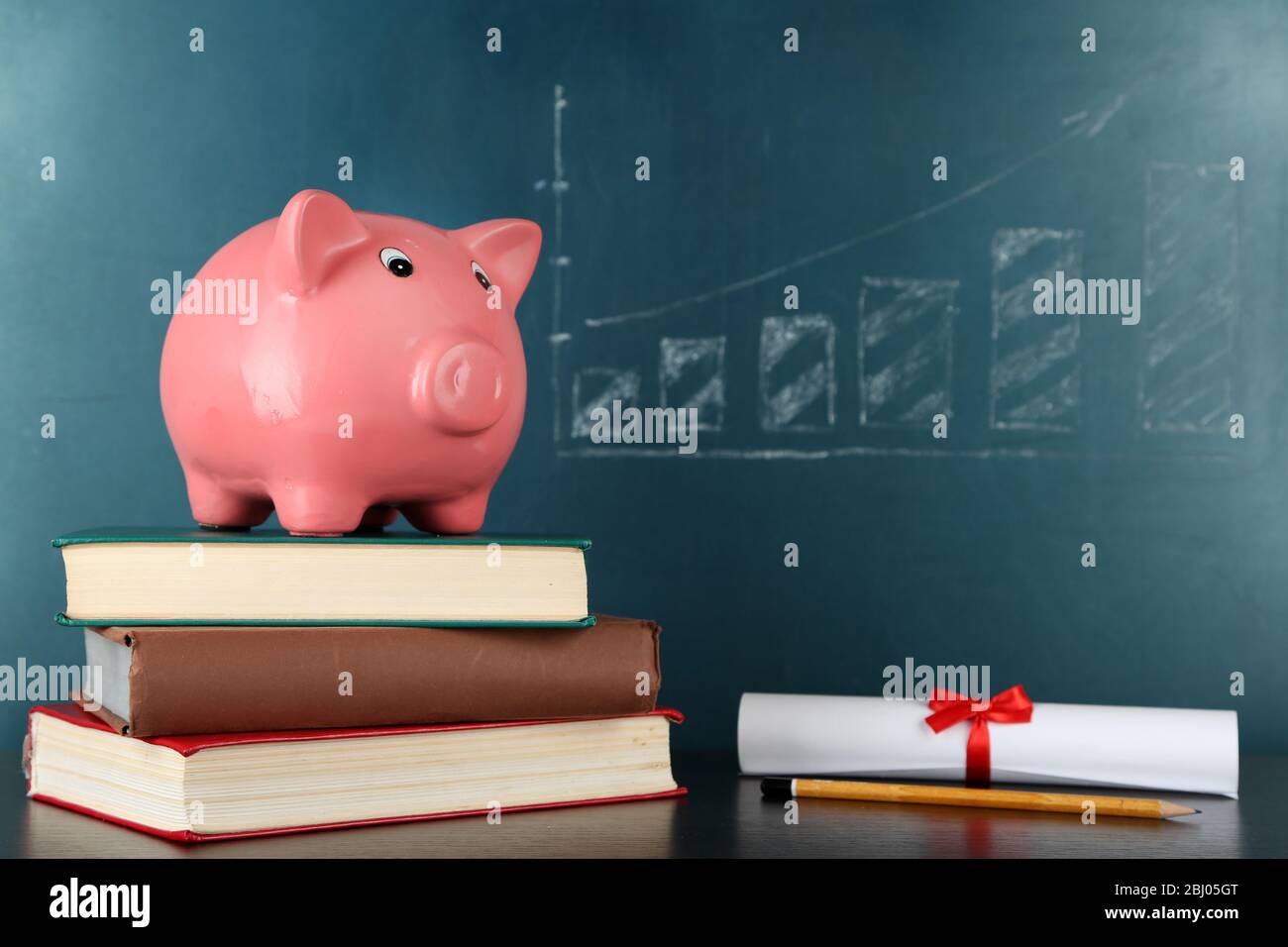 Piggy bank with books on blackboard background Stock Photo - Alamy
