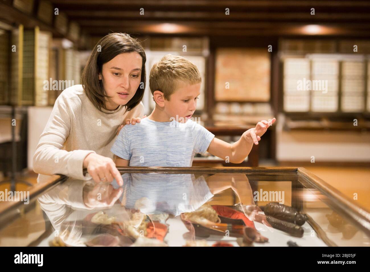 Young woman with son observing with interest exhibition under glass in ...