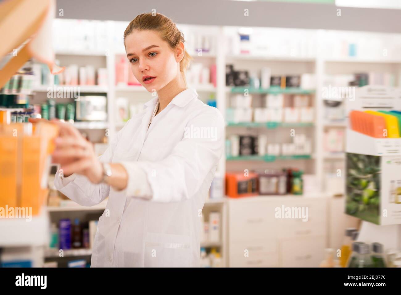 Positive pharmacist is browsing rows of body care products in pharmacy ...