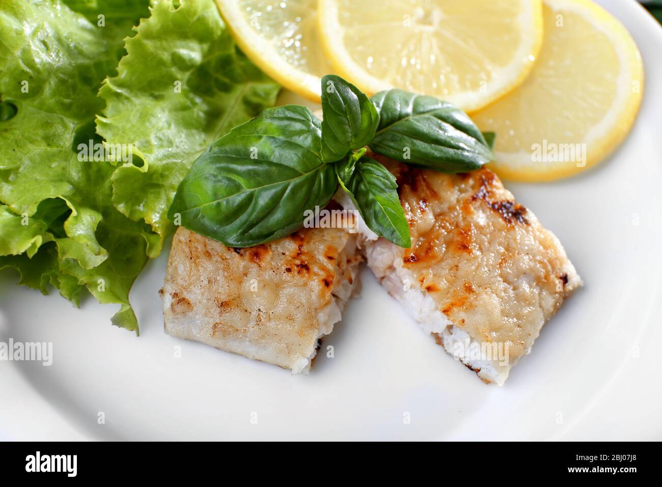 Dish of fish fillet with greens and lemon on plate close up Stock Photo ...