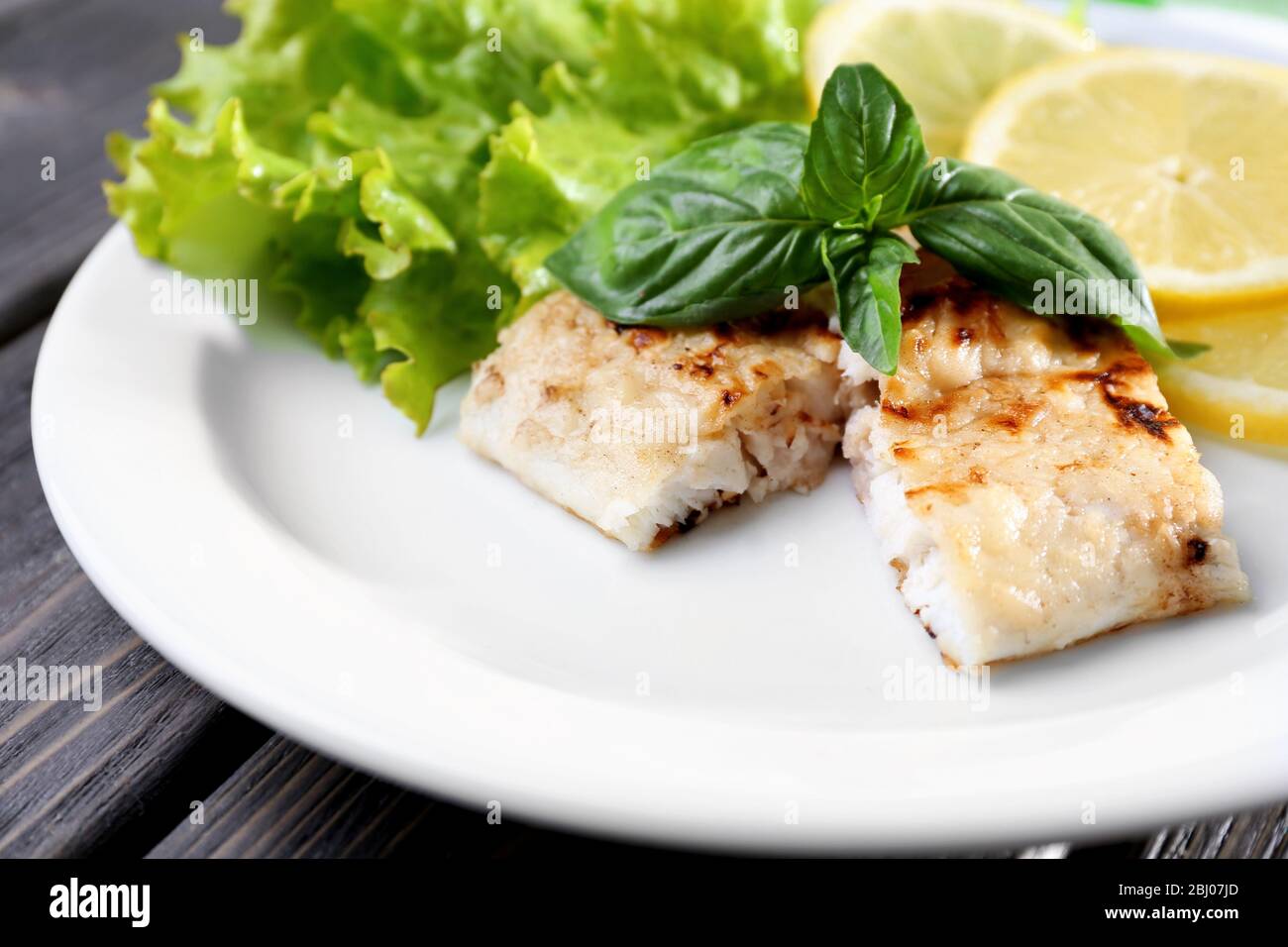 Dish of fish fillet with greens and lemon on plate close up Stock Photo ...