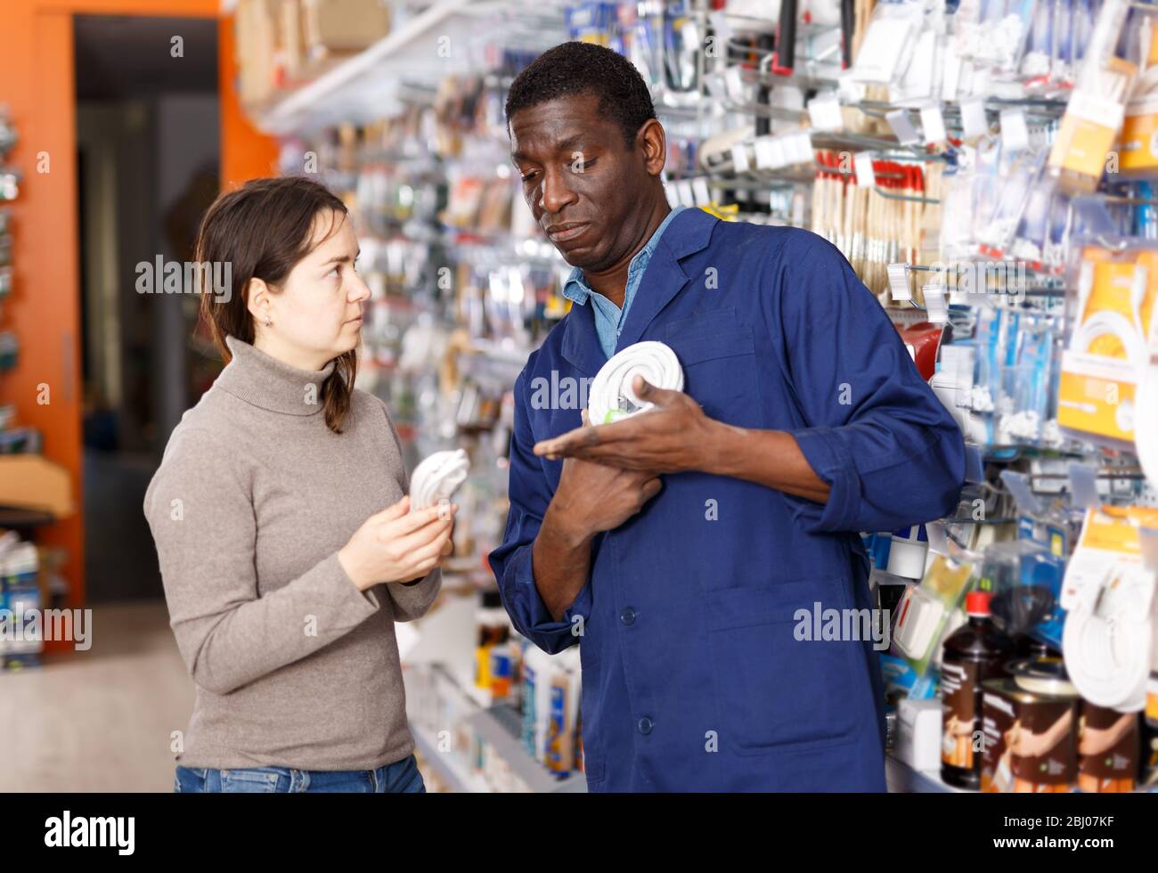 Modern salesman offering materials and tools to young woman in shop of ...