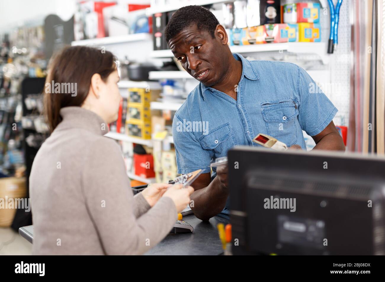 Happy salesman offering materials and tools to young woman in shop of ...
