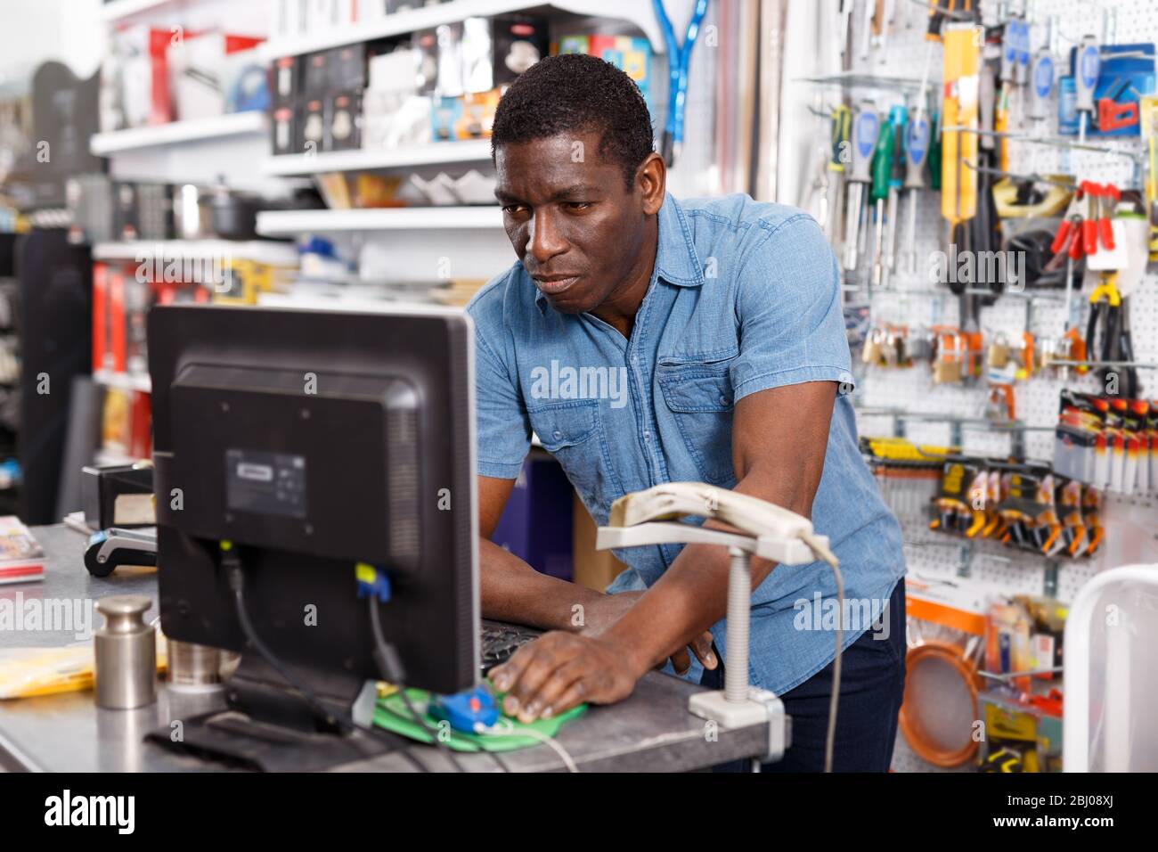 Adult African American salesman working on computer behind counter in ...
