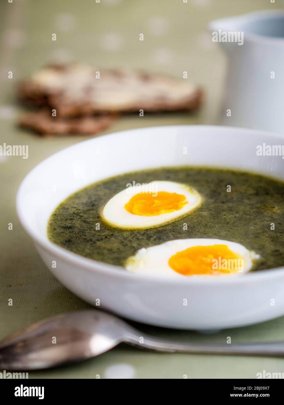 White bowl of Swedish nettle soup on striped cloth with silver spoon ...