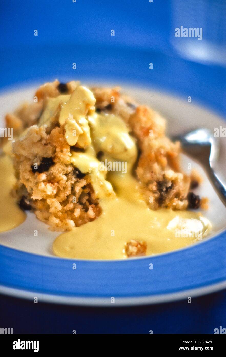Portion of fruit crumble with custard poured over on blue edged plate ...