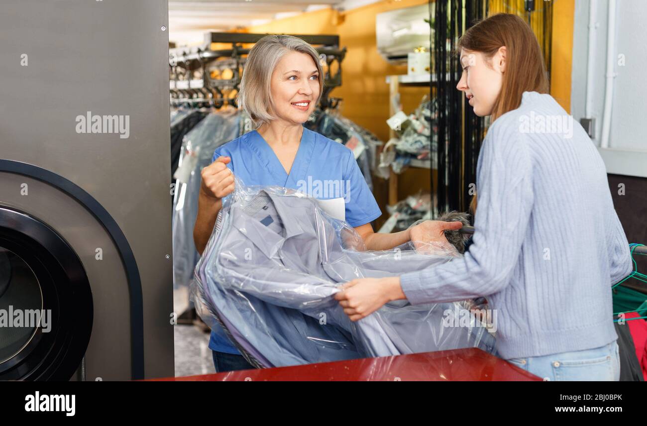 Glad positive female client receiving her clean clothes at dry-cleaning ...