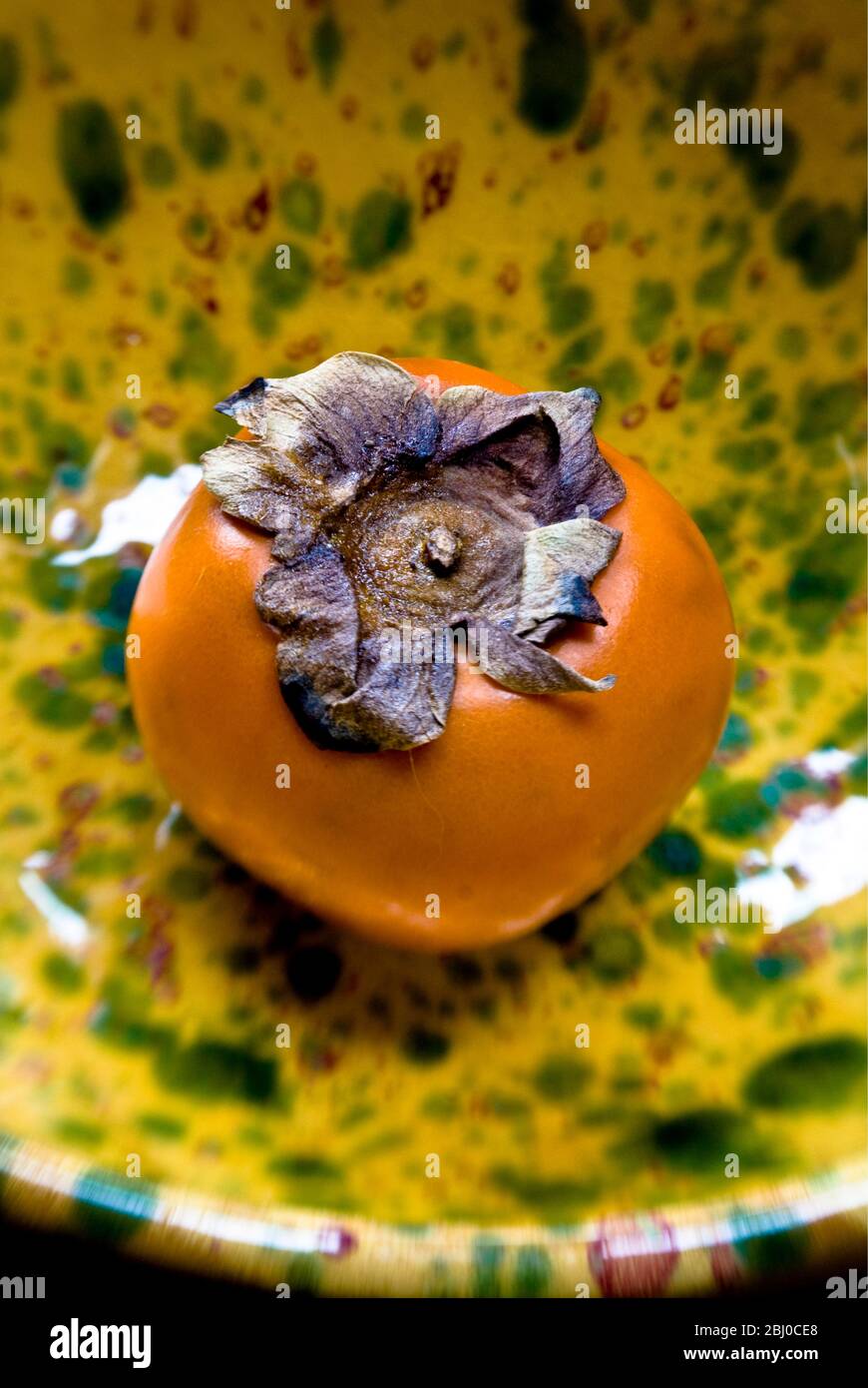 Single red persimmon (sharon) fruit on spatter painted bowl Stock Photo ...