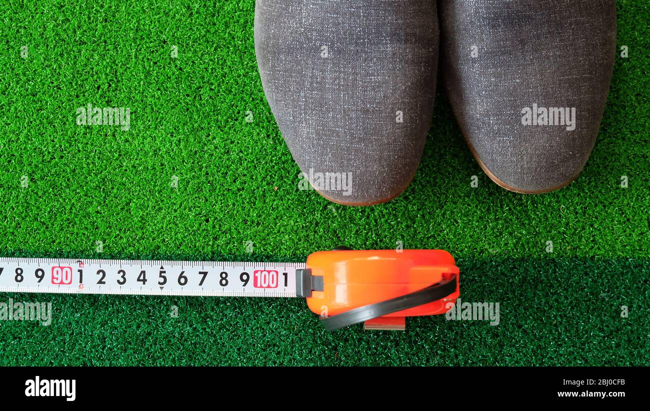 The tip of a pair of gray shoes with a measuring tape in front, showing ...