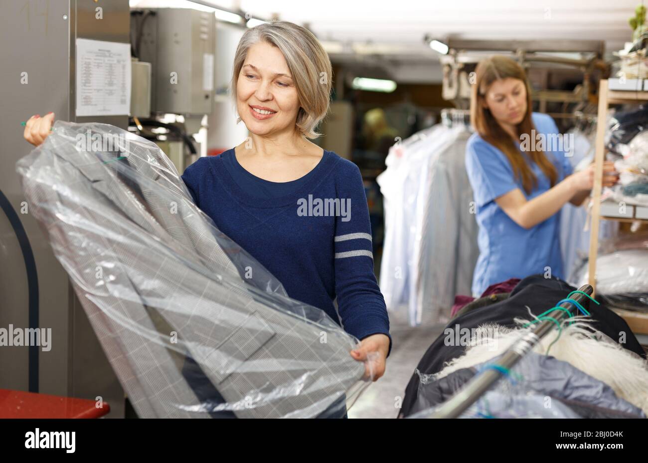 Portrait of satisfied female customer holding her clean clothes at dry ...