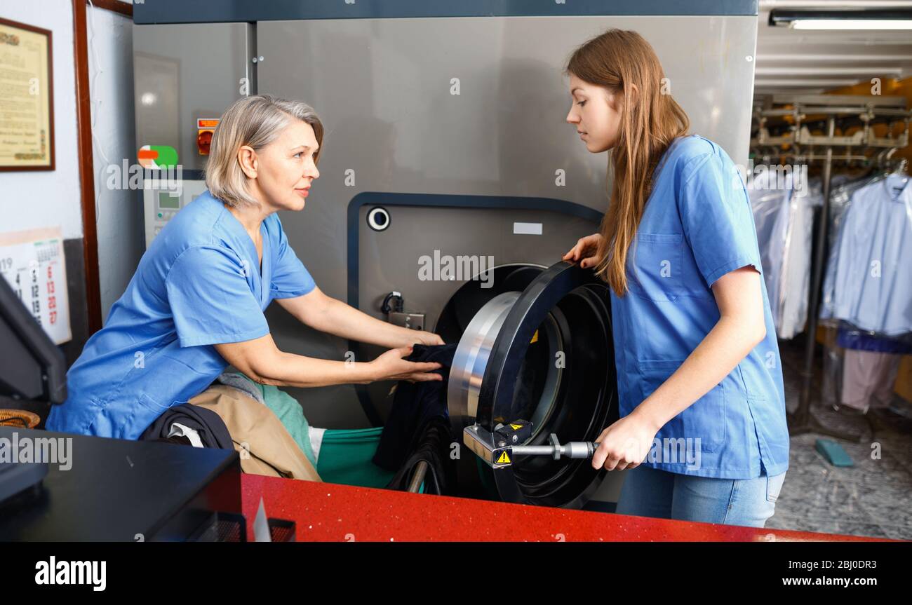 Two efficient glad women in uniform working at laundry and taking out ...
