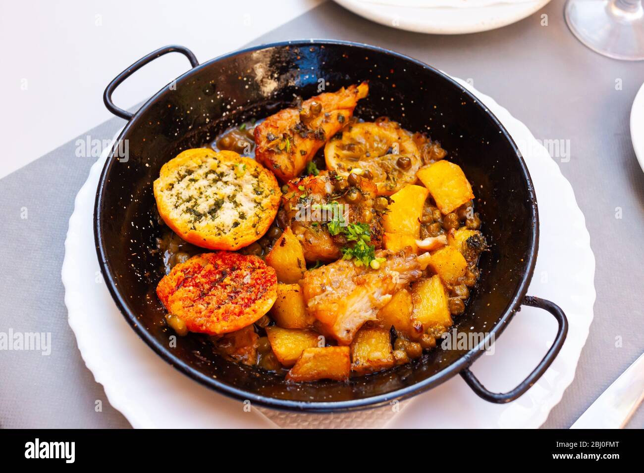 Baked monkfish fillet with lemon, vegetables and toasted bread in iron ...