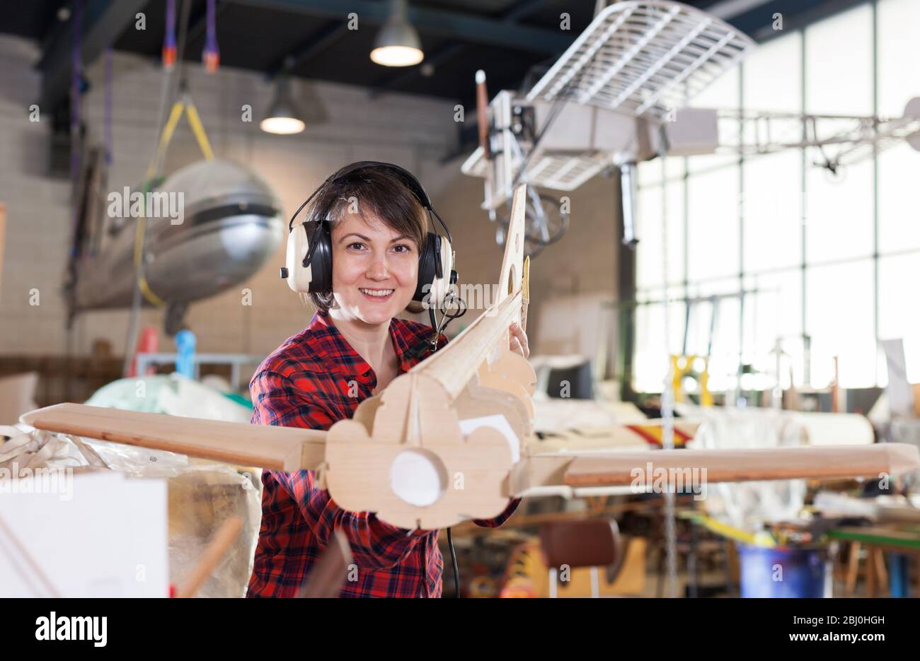 Portrait of happy female hobbyist in aviator headphones with unfinished ...