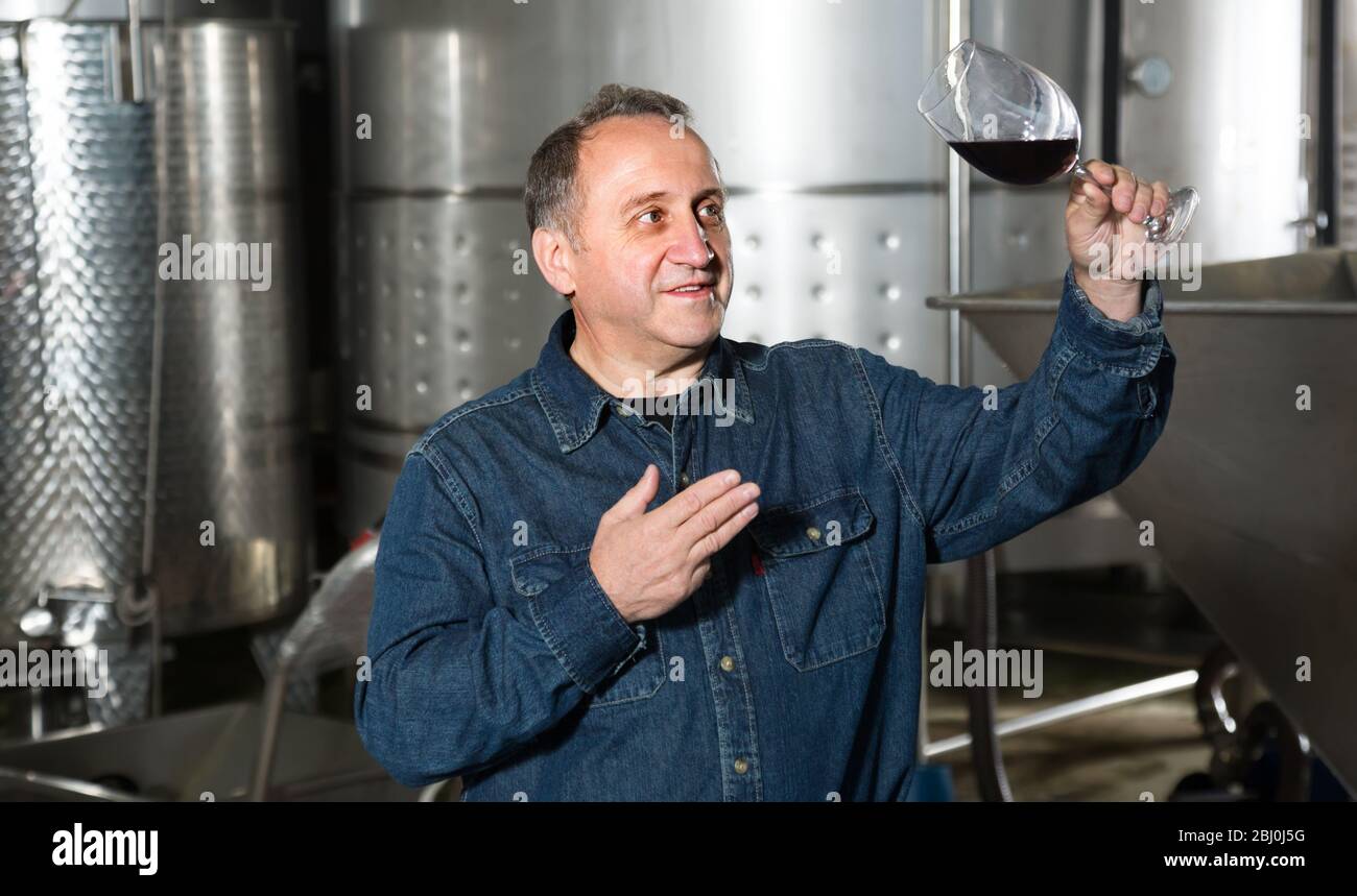 Elderly worker of winery tasting wine near tanks Stock Photo - Alamy