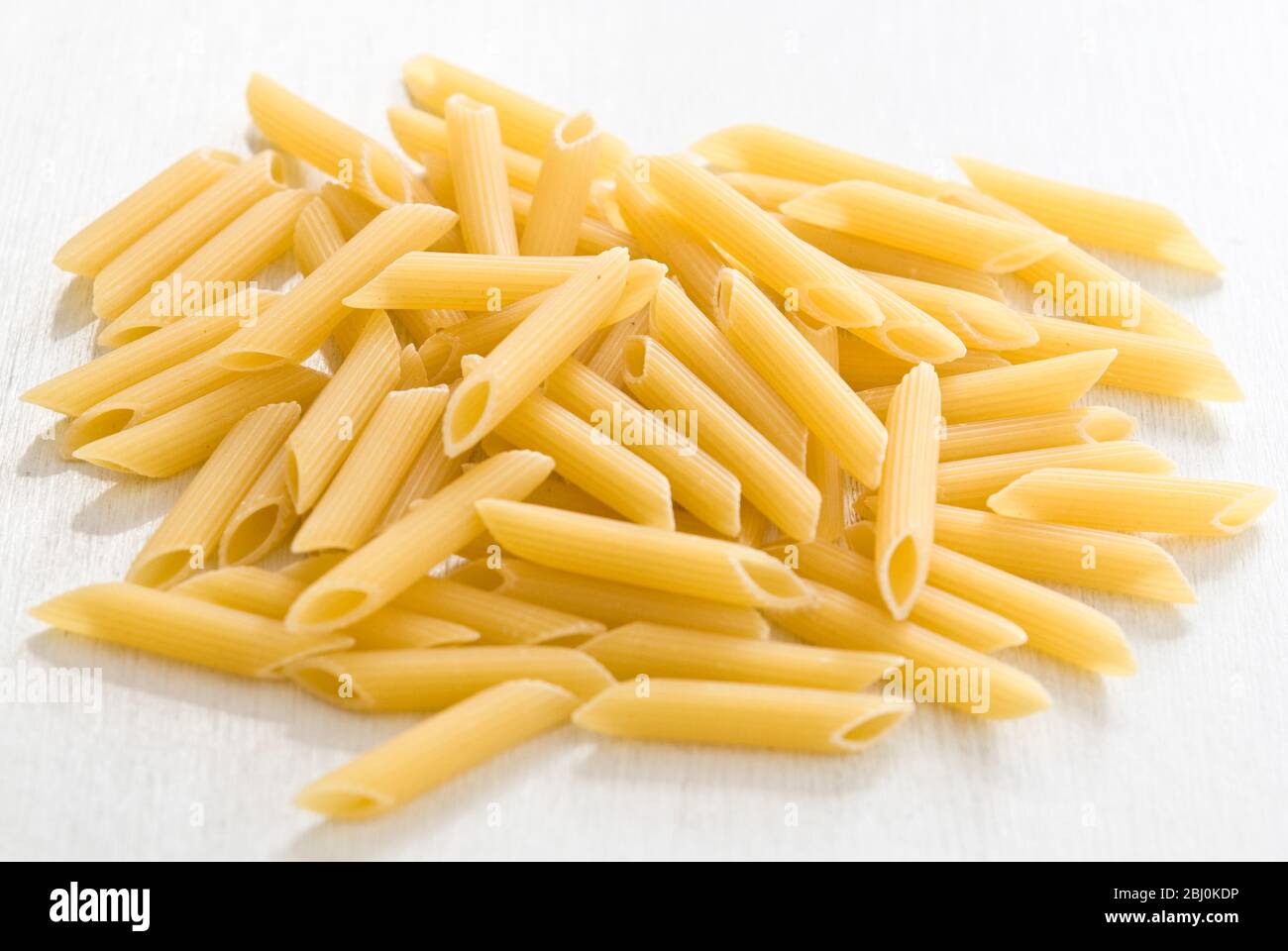 Pile of penne, uncooked dried pasta shapes on white surface Stock Photo ...