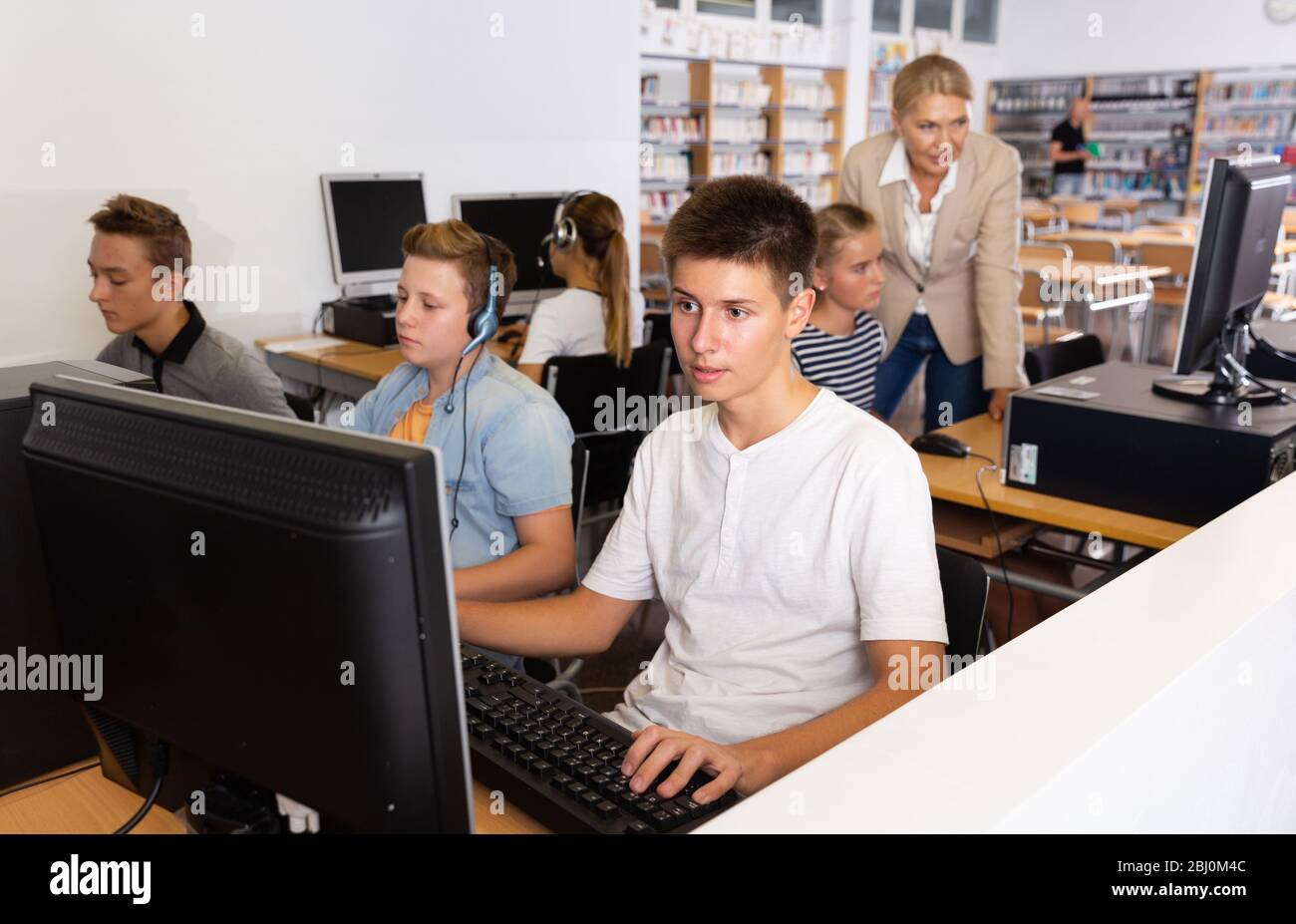 Schoolchildren and female teacher working with computers in classroom ...