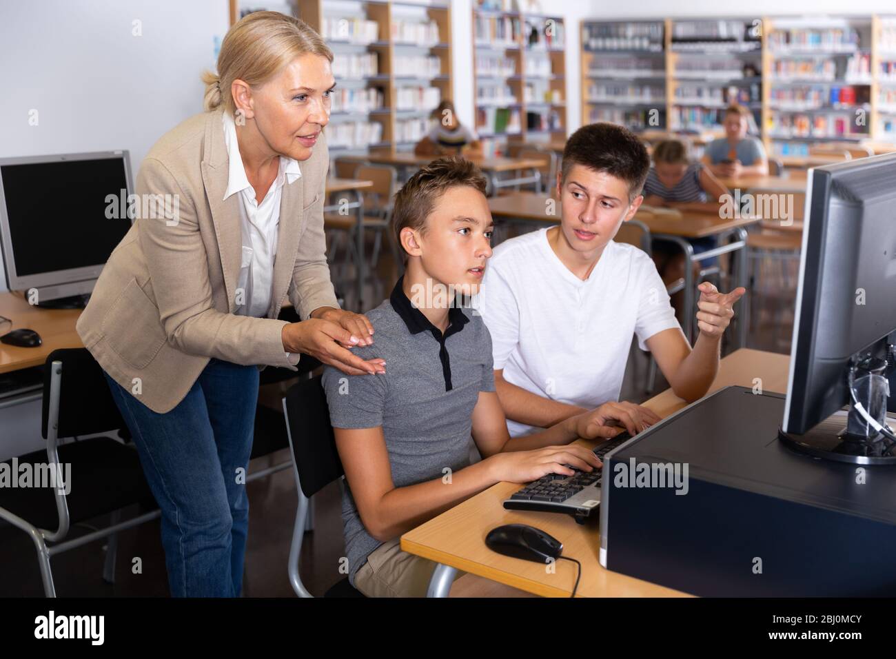 Schoolchildren and adult female teacher working with computers in ...