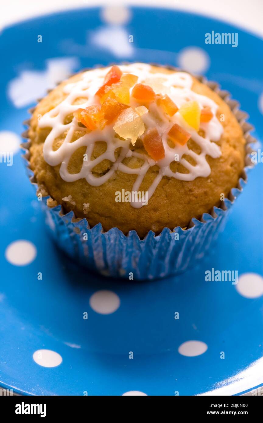 Muffin decorated with squiggly icing and candied peel on spotted blue ...
