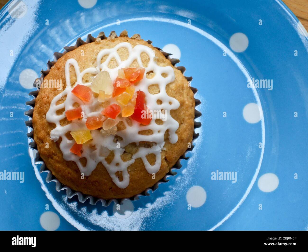 Muffin decorated with squiggly icing and candied peel on spotted blue ...