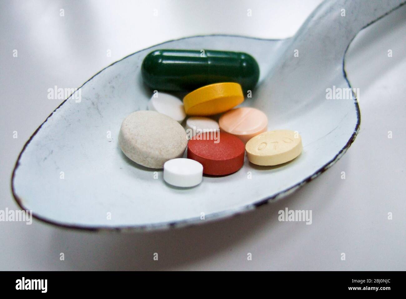 White enamel spoon of various coloured pills Stock Photo - Alamy