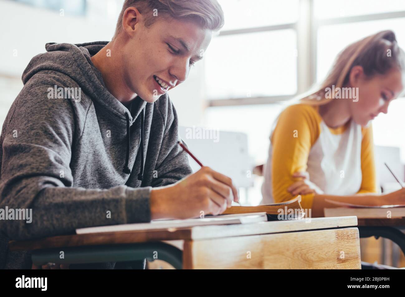 Teenage boy sitting in high school classroom writing in book. Male ...